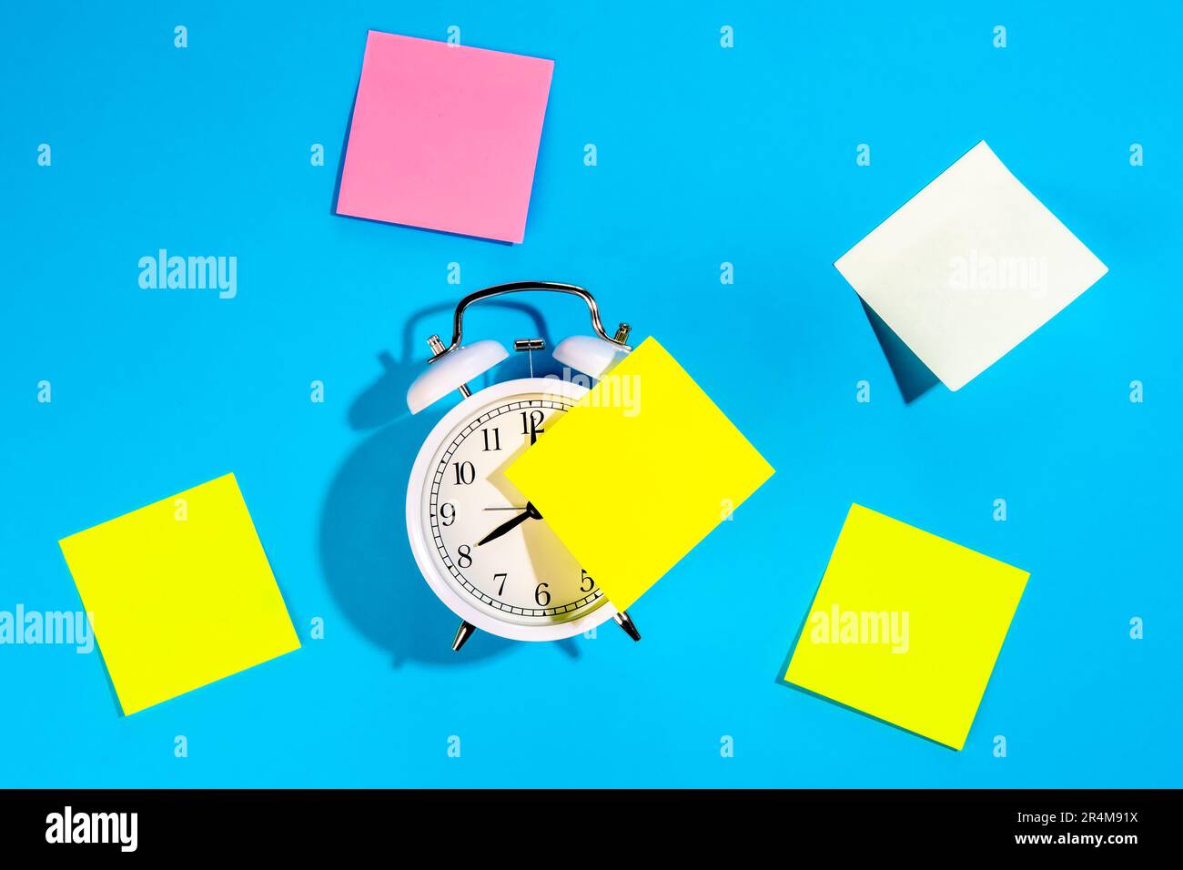 Alarm clock and colorful blank paper reminders on a blue background ...