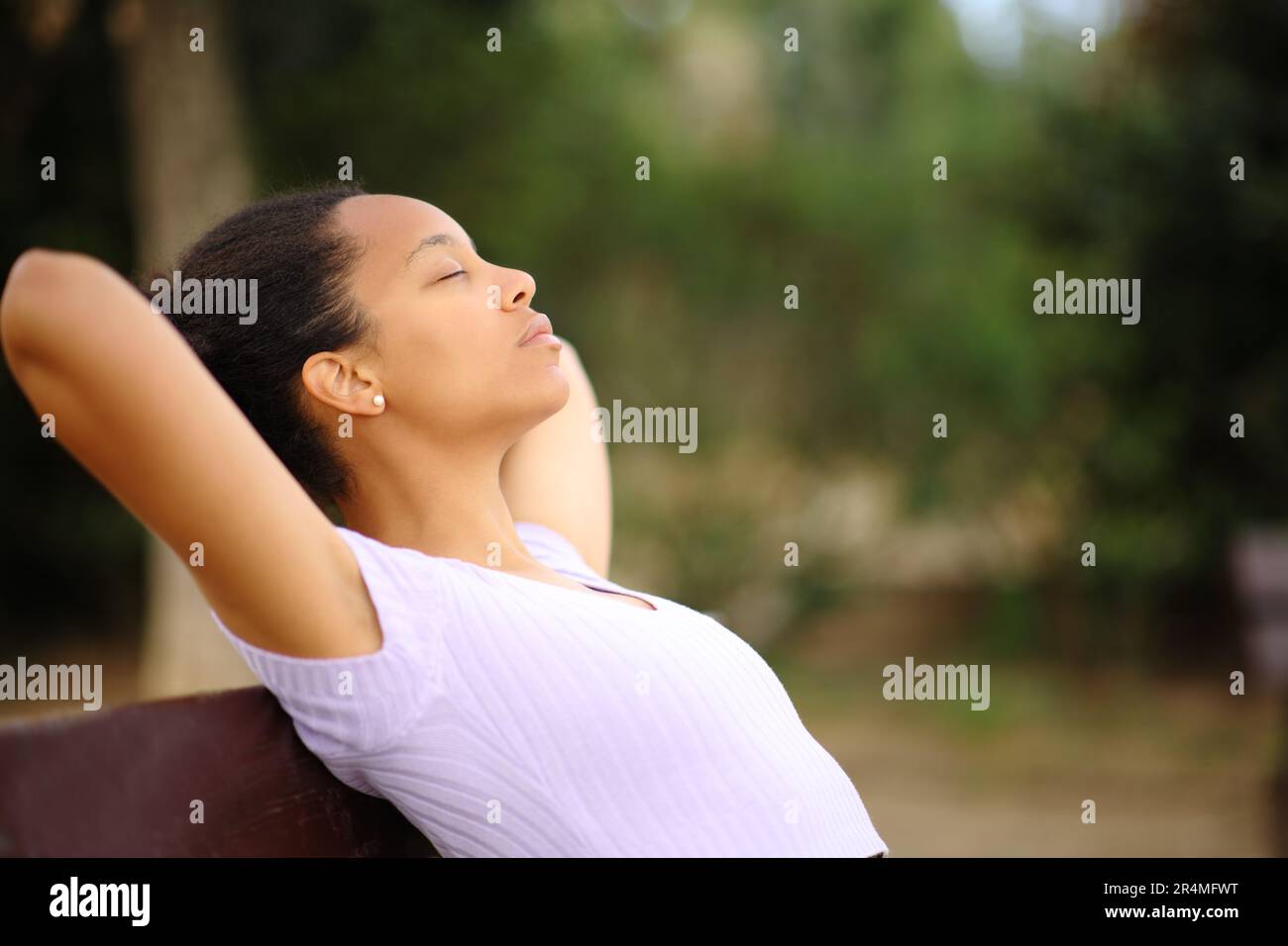 Profile of a relaxed black woman resting with hands on head sitting in ...