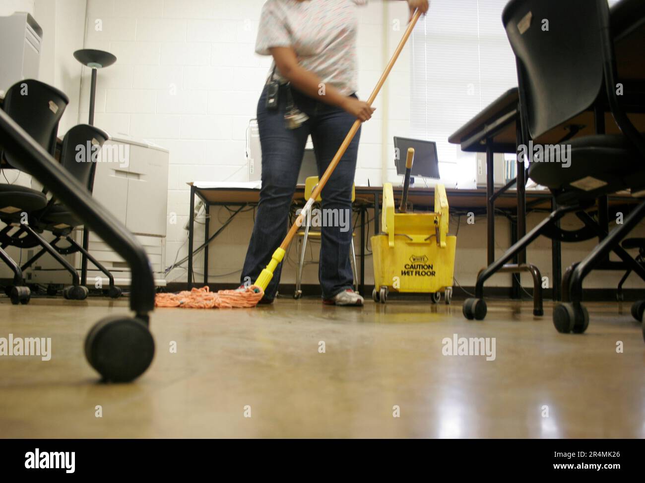 A female janitor sweeps the floor with a broom and dustpan in a ...