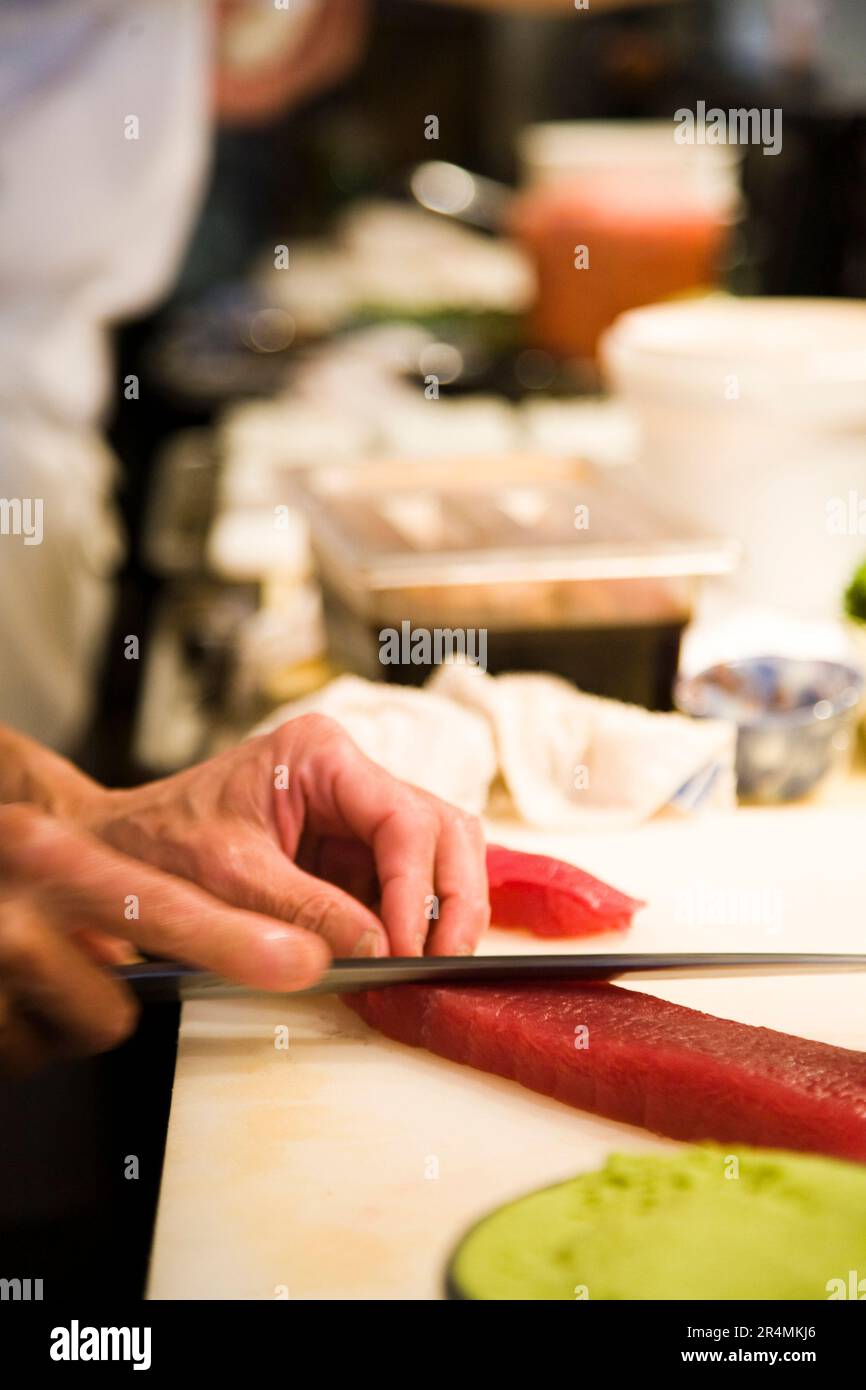 A detail of a man slicing a fresh slice of tuna at a sushi restaurant ...