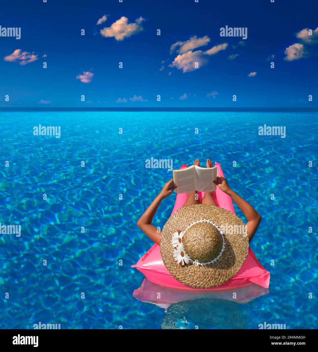 A woman reading a book in an infinity pool overlooking a clear blue sky ...