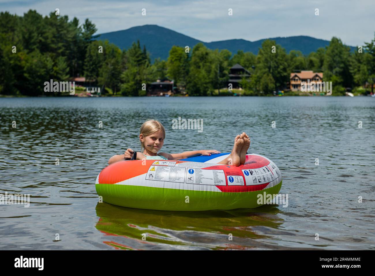 Girl floating in lake on tube with mountains and trees in background ...