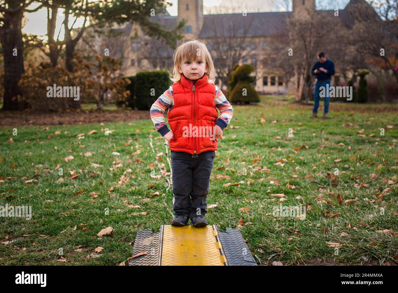 A little child stands determined with hands on hips, dad in background ...