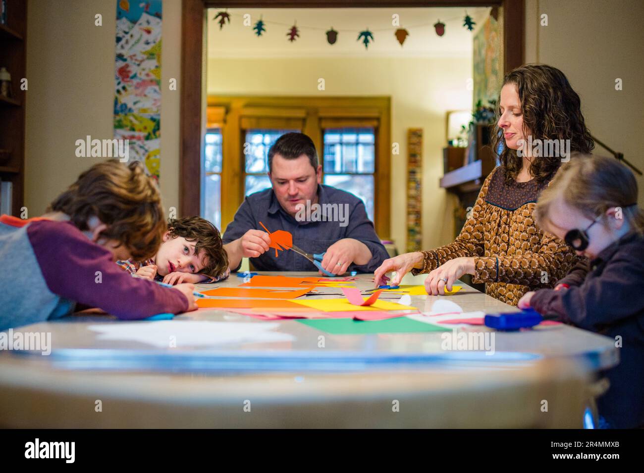 A family sit together at a dining room table creating paper craft art ...
