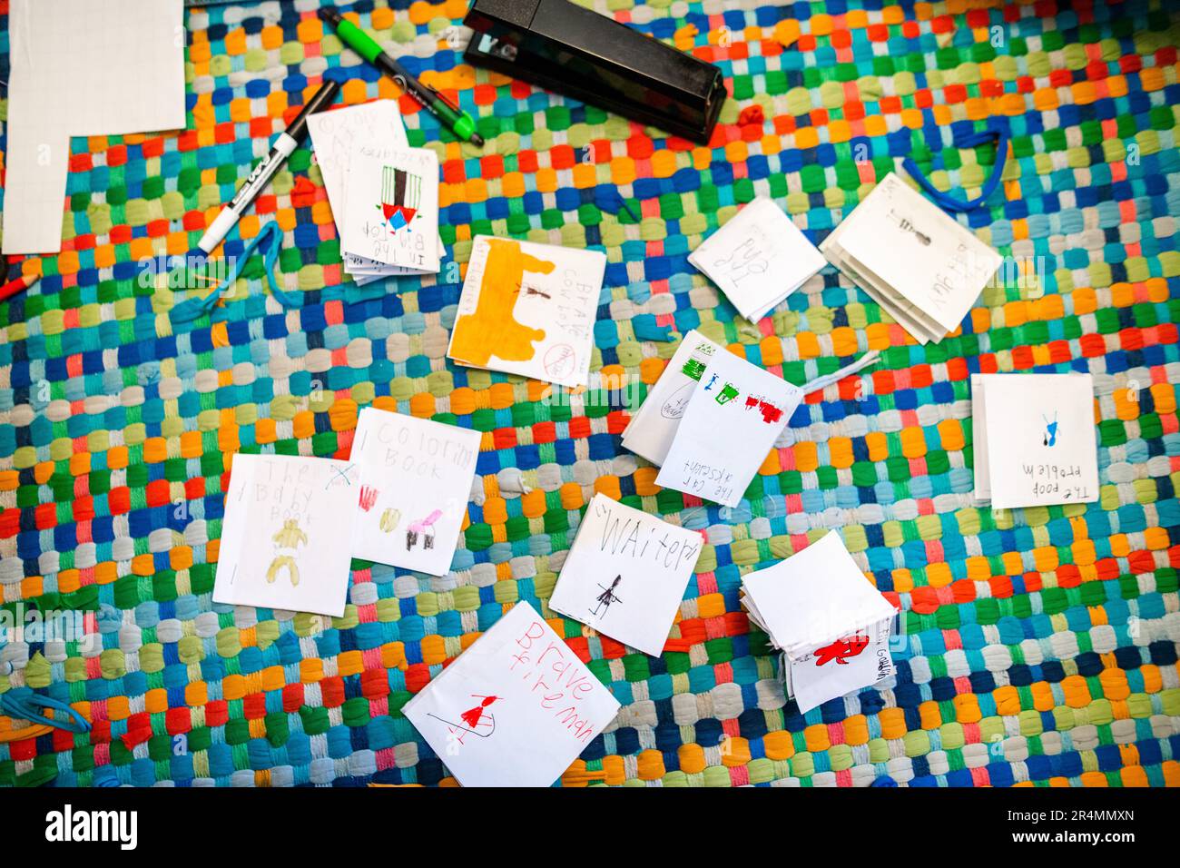 Little books created by a small child are spread across a colorful rug ...