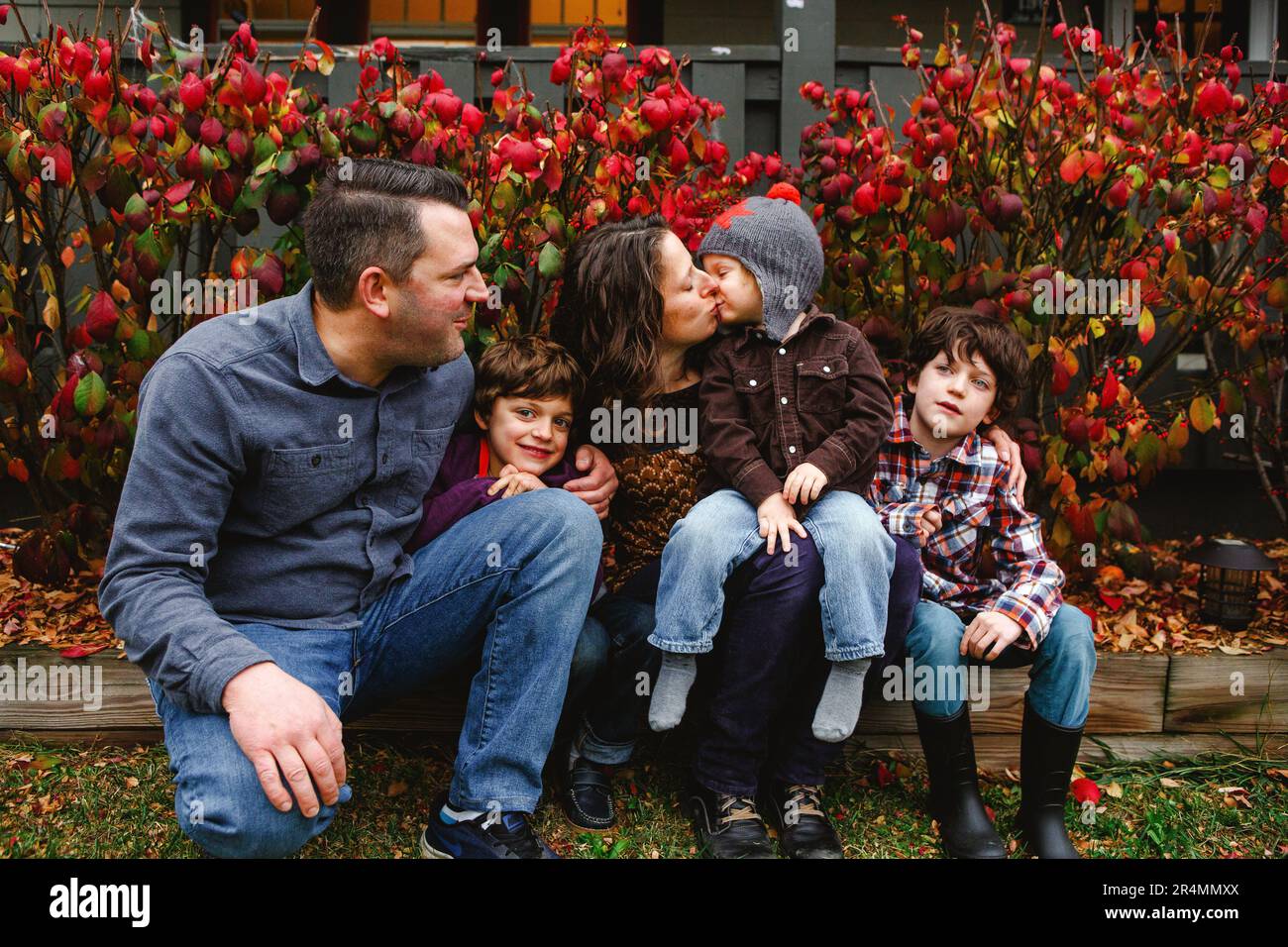 A mom kisses a little boy in her lap while their family fondly look on ...