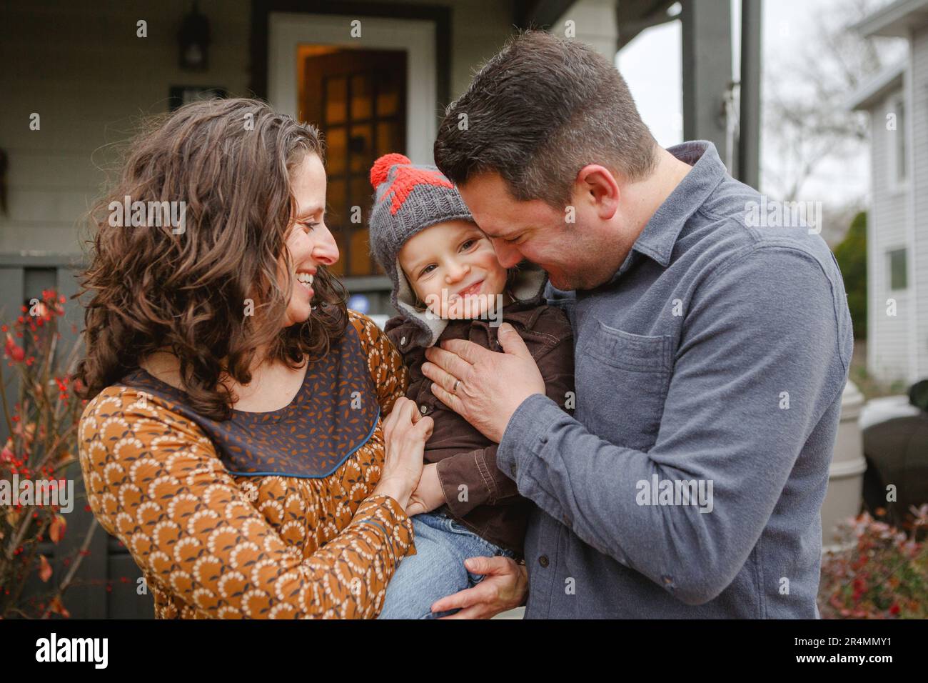 A joyful child is being tenderly held between his mom and dad in yard ...