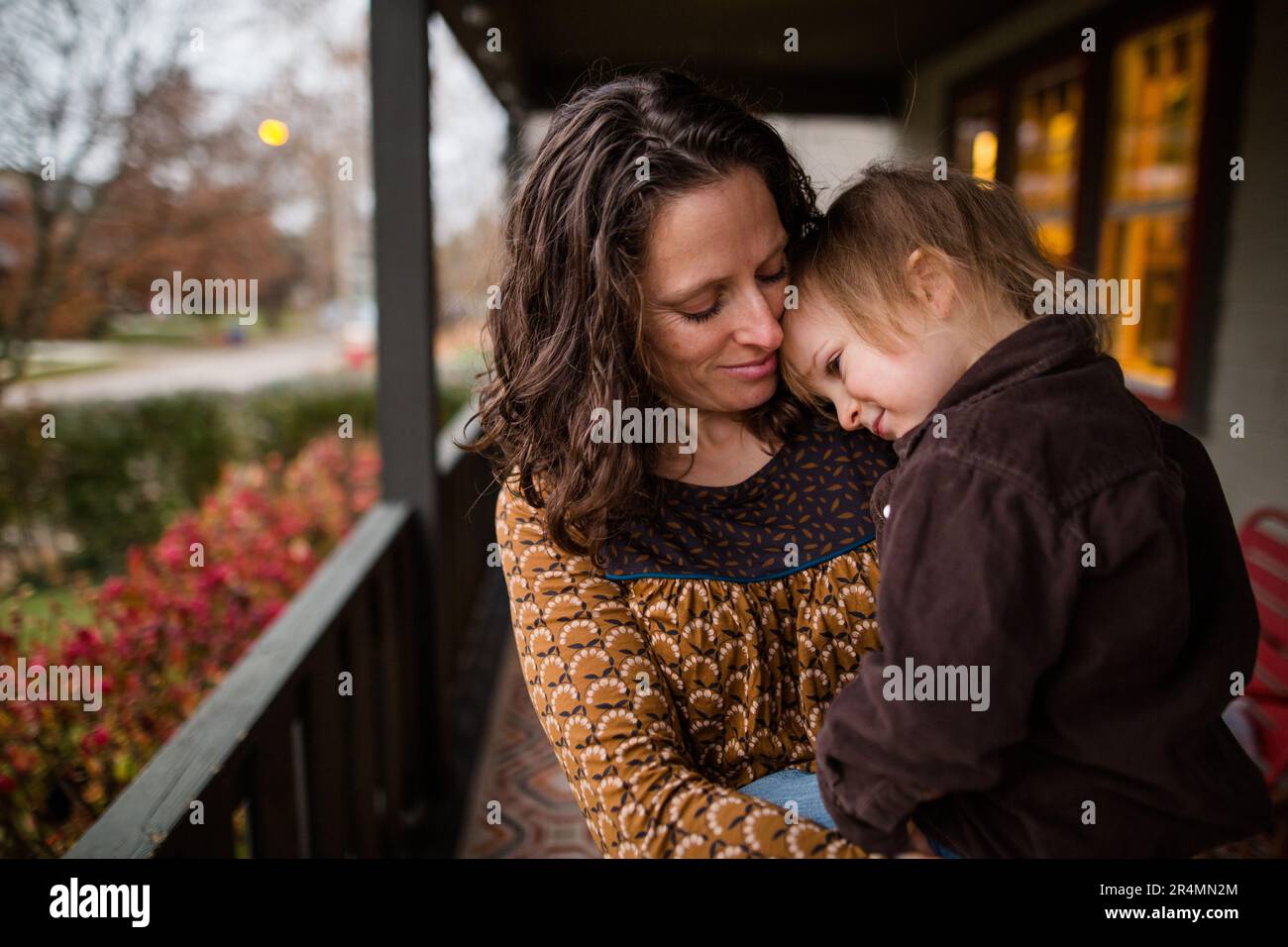 a smiling mother and child cuddle quietly together on porch in evening ...