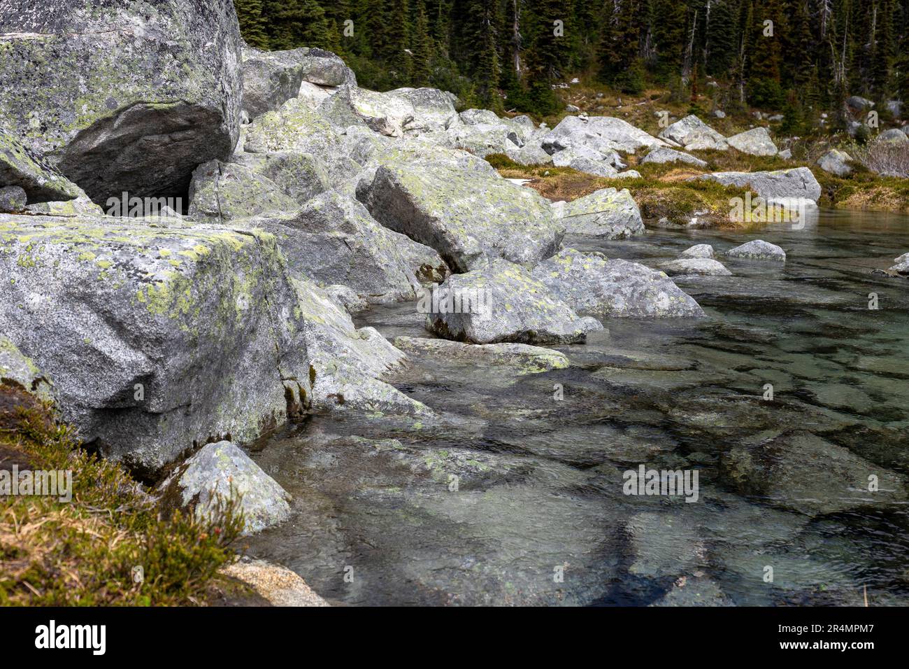 Water flows out from underneath boulders into a lake in the mountains ...