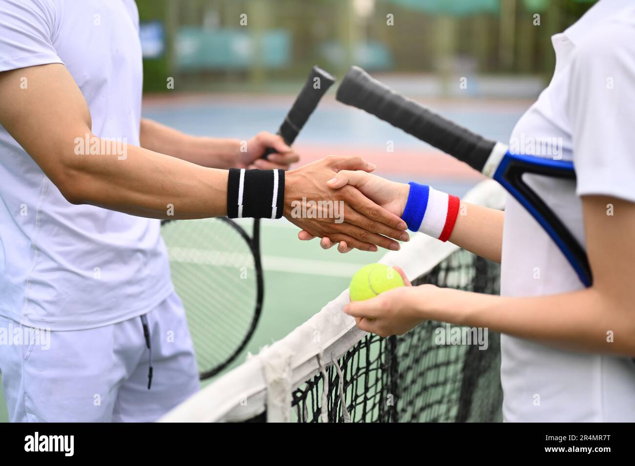 Male and female tennis players shaking hands over net at tennis court ...