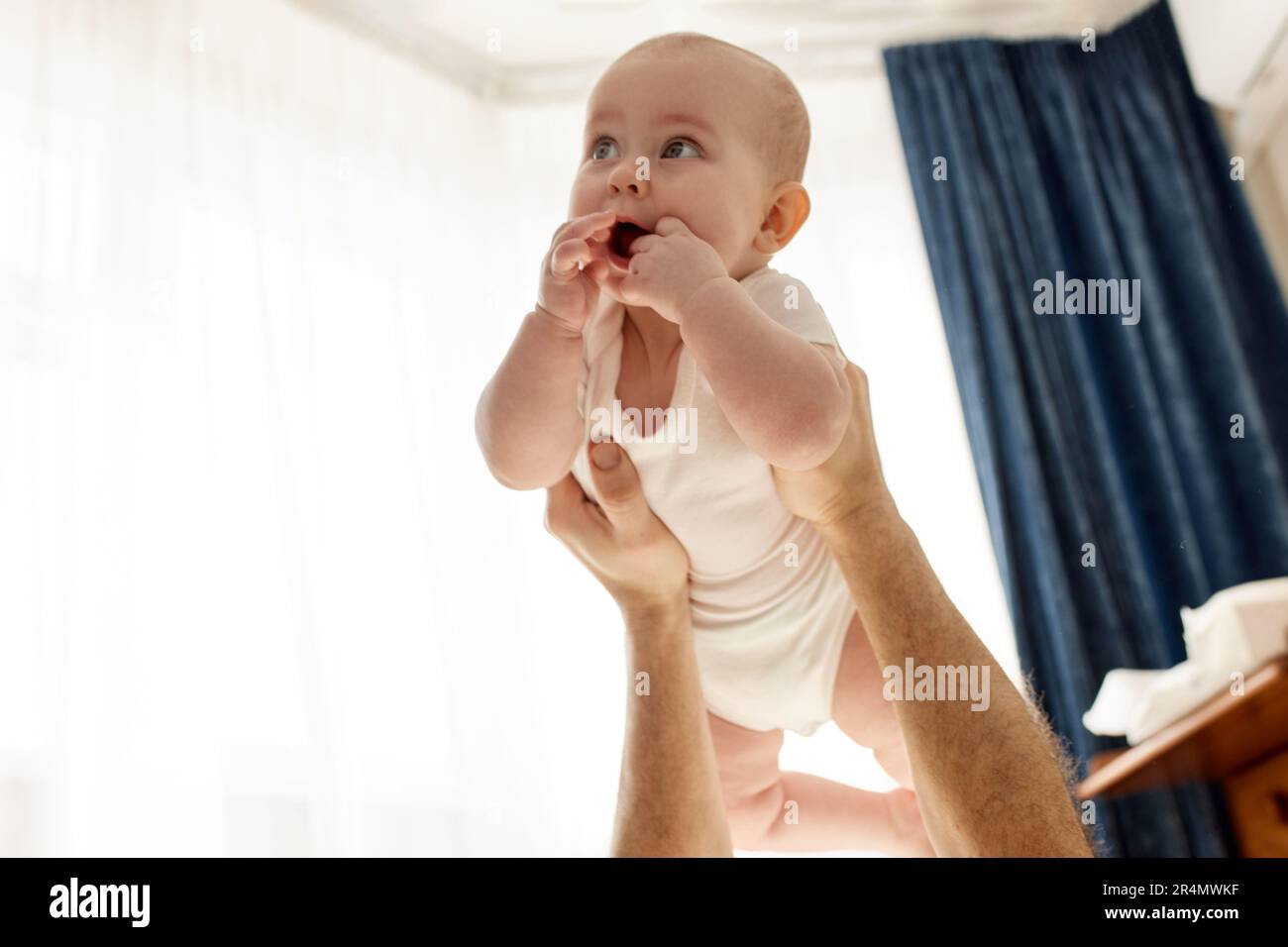 A cute joyful smiling baby on the outstretched arms of his father, who ...