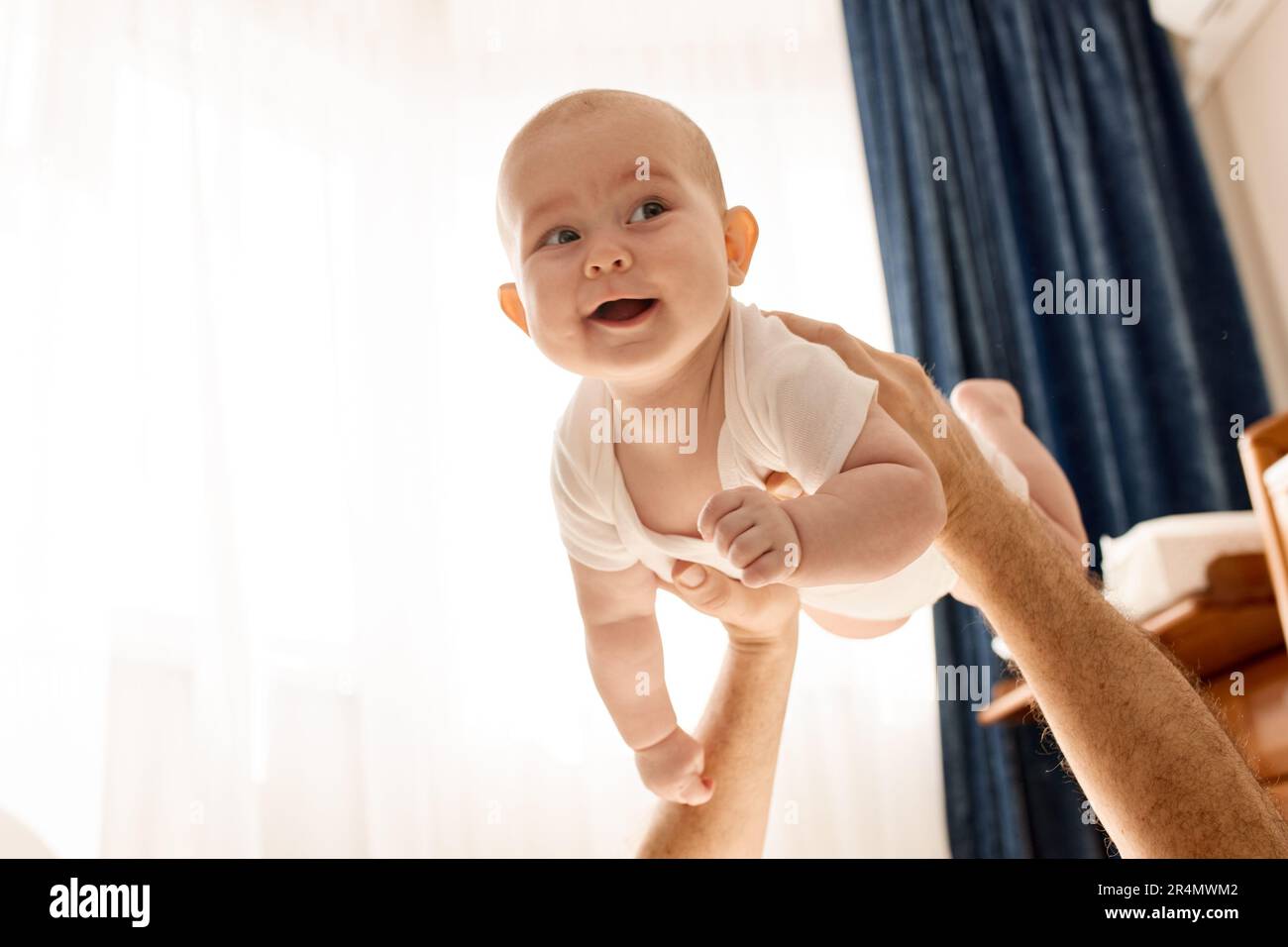 A cute joyful smiling baby on the outstretched arms of his father, who ...