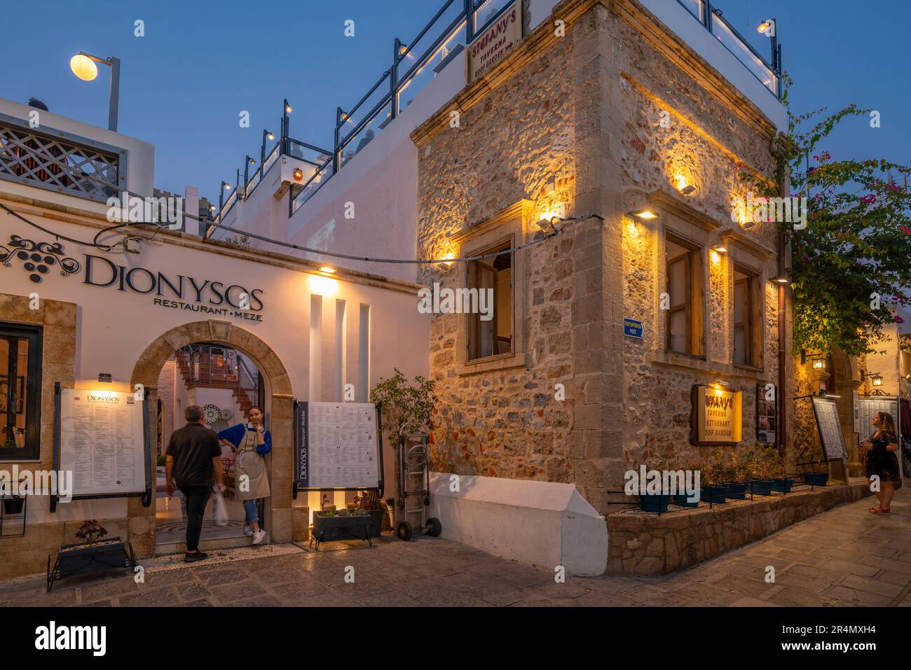View of bar in Lindos street at dusk, Lindos, Rhodes, Dodecanese Island ...
