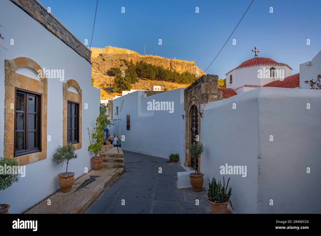 View of Lindos Acropolis from whitewashed street in town at sunset ...