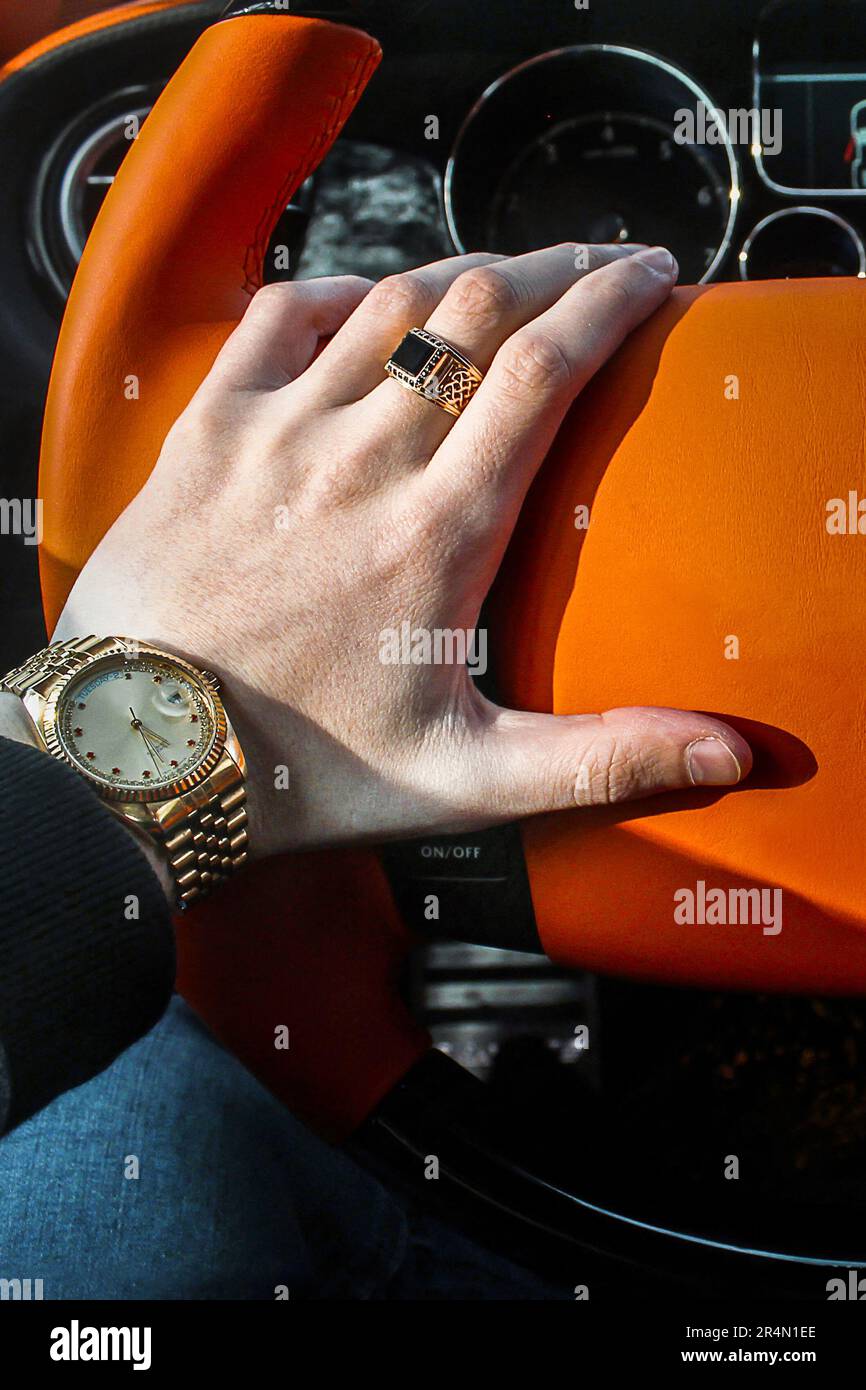 A man holds the steering wheel of a luxury car. Gold watch and a ring ...