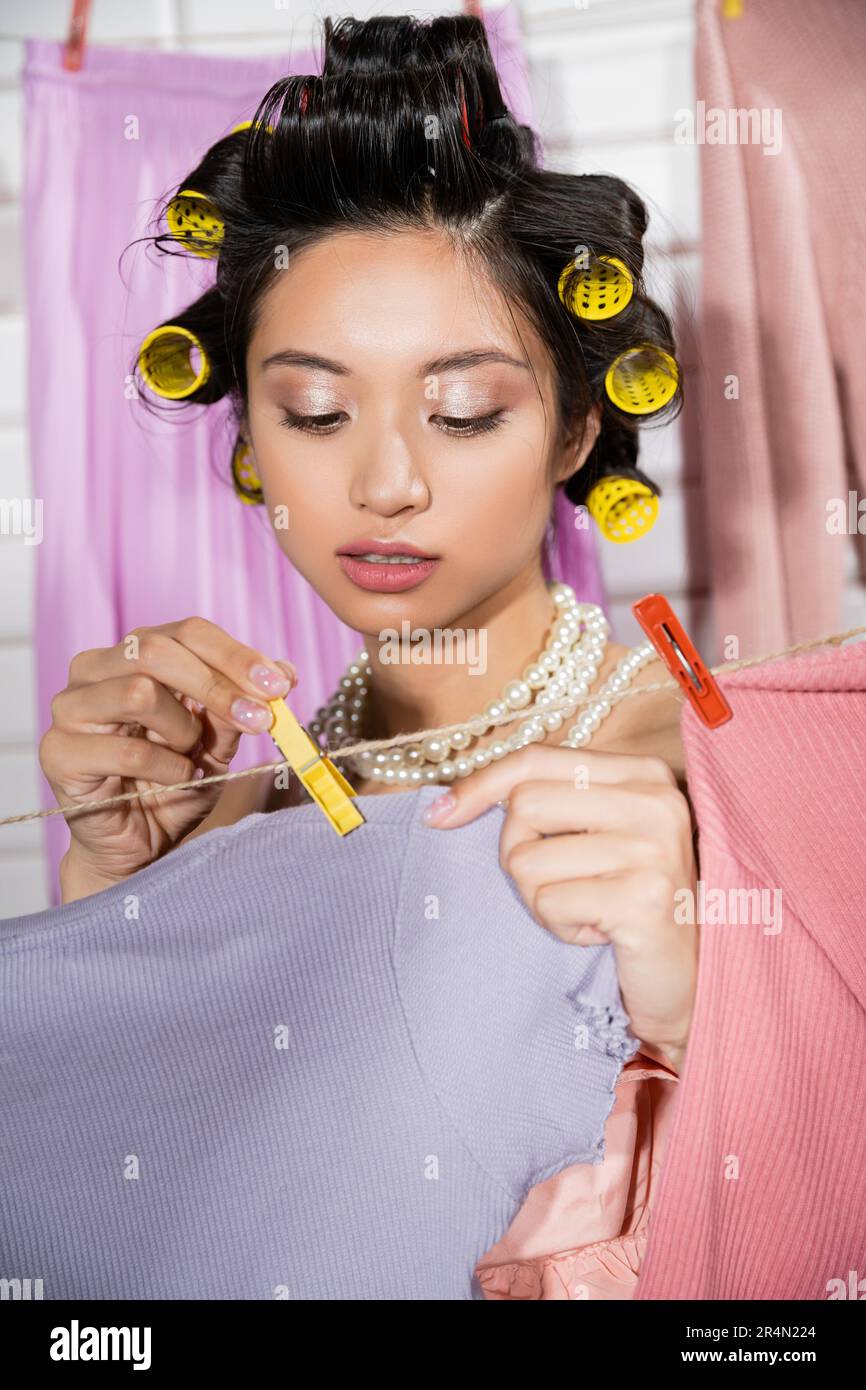 young asian woman with hair curlers and pearl necklace holding clothes ...