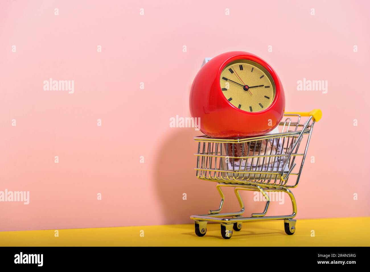 A supermarket trolley with old vintage alarm clock on pink and yellow ...