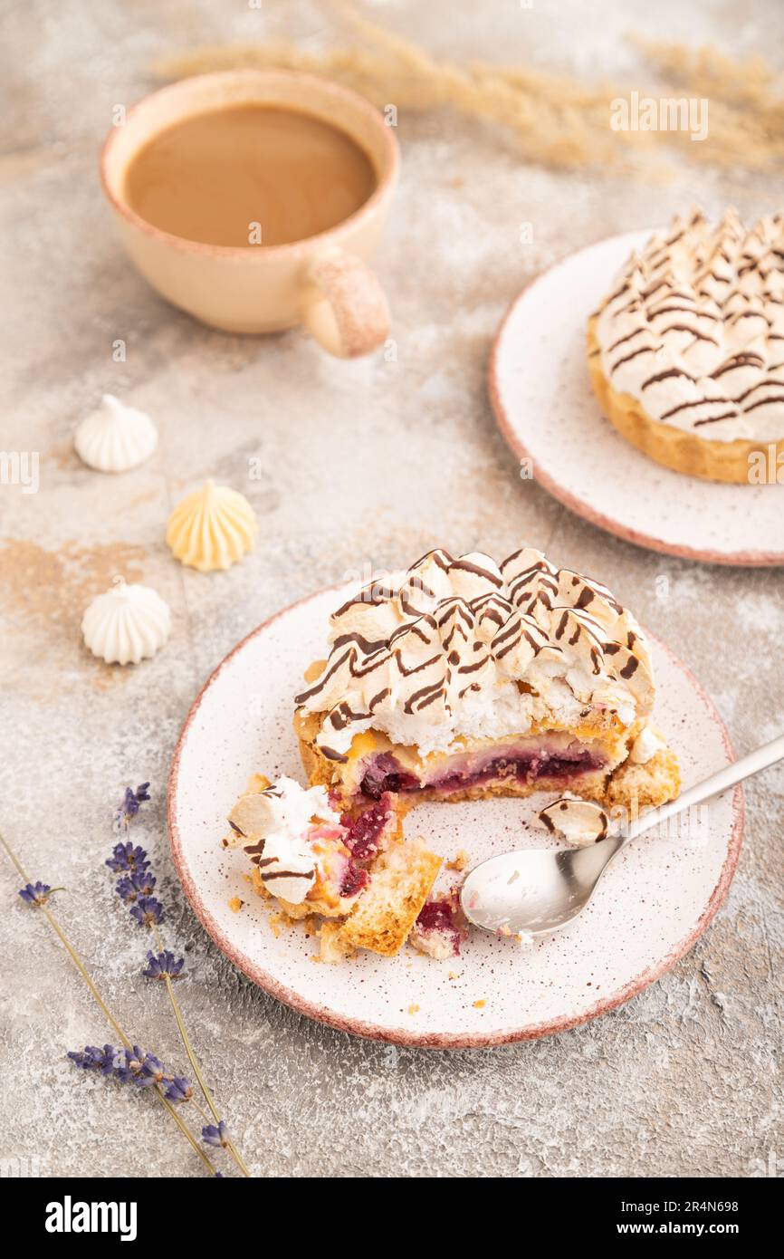 Two tartlets with meringue cream and cup of coffee on brown concrete ...