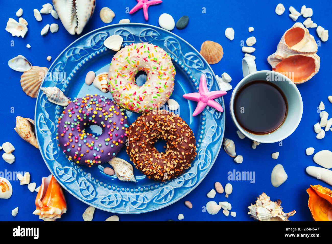 Assorted donuts in a plate on a blue background. Around them are symbols of the sea - shells ...