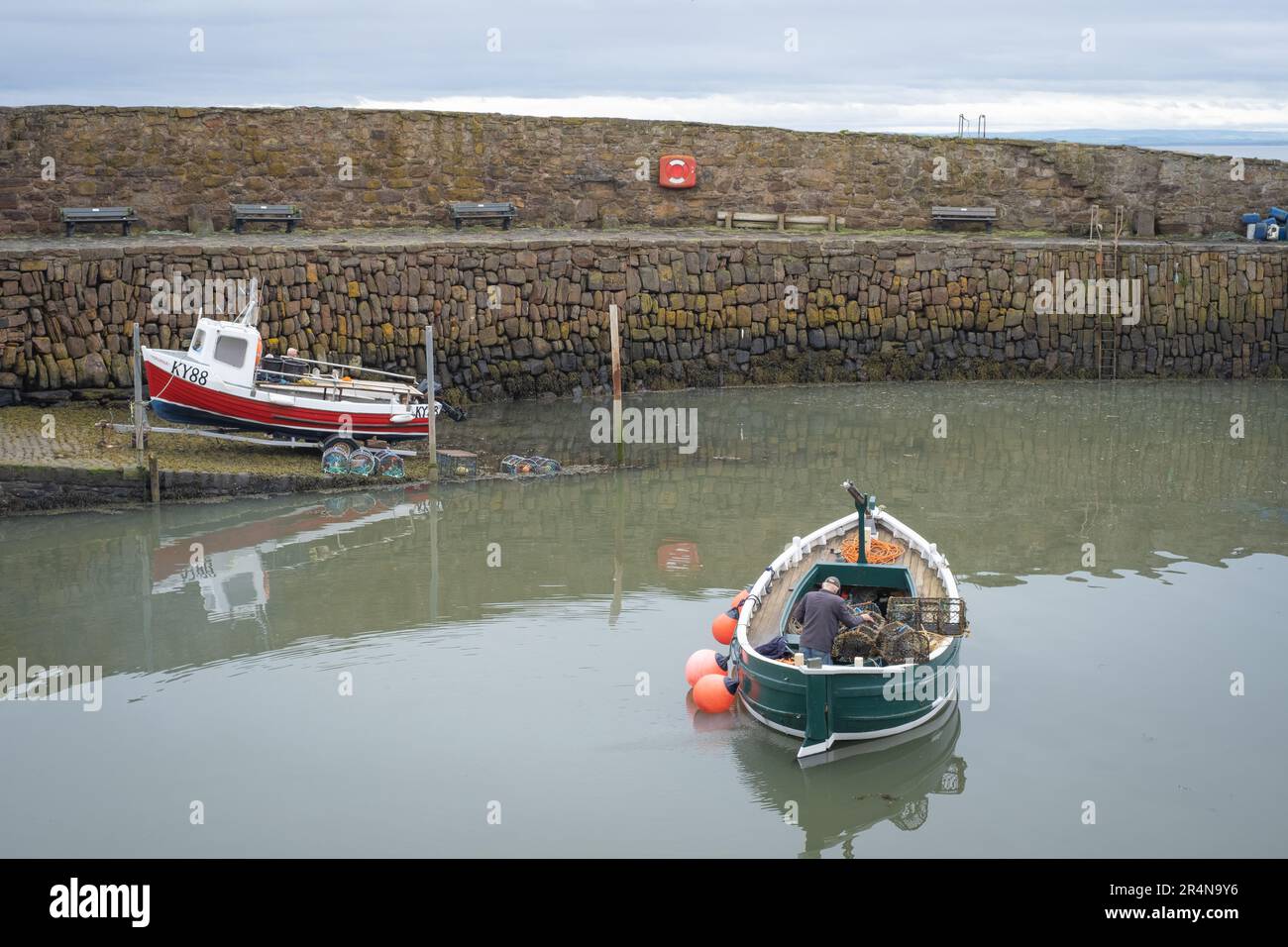 Elderly fisherman moves his small boat with lobster pots in Crail ...
