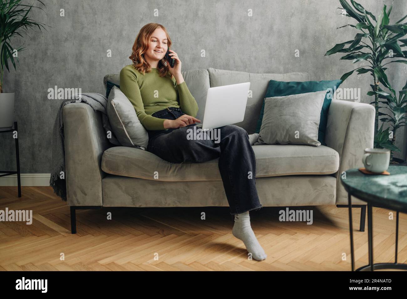 Happy relaxed young woman sitting on couch using cell phone, smiling ...