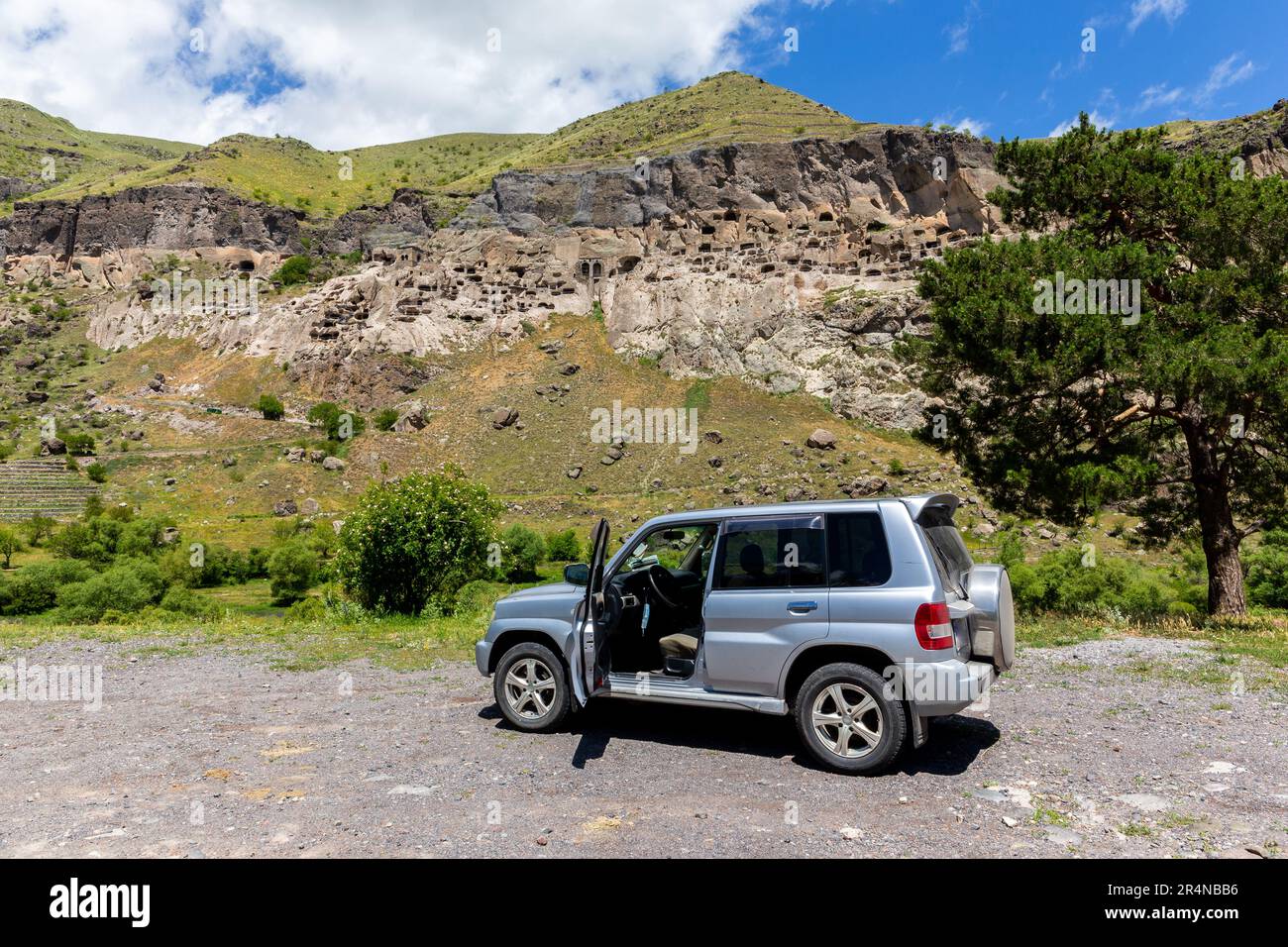 Off-road 4x4 car parked on a gravel road with Vardzia cave monastery ...