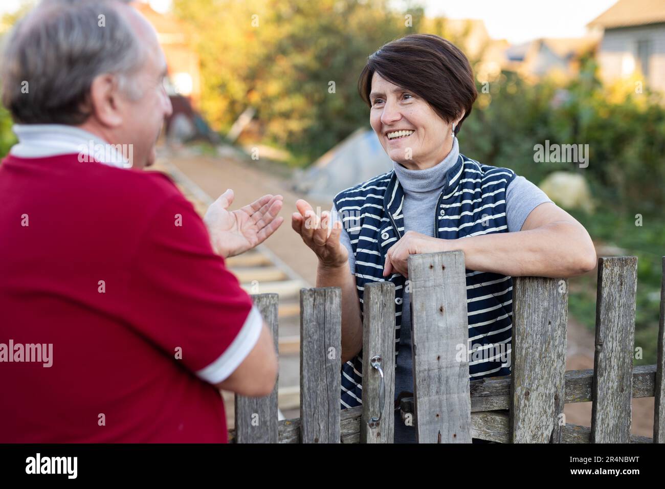 Neighbors standing at fence outdoors and having conversation. Village ...