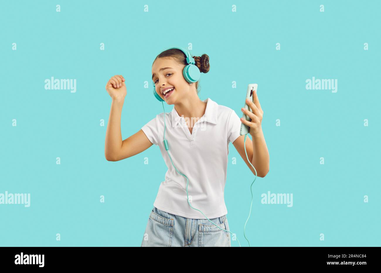Young cute Caucasian girl teen in headphones holding phone and dancing ...