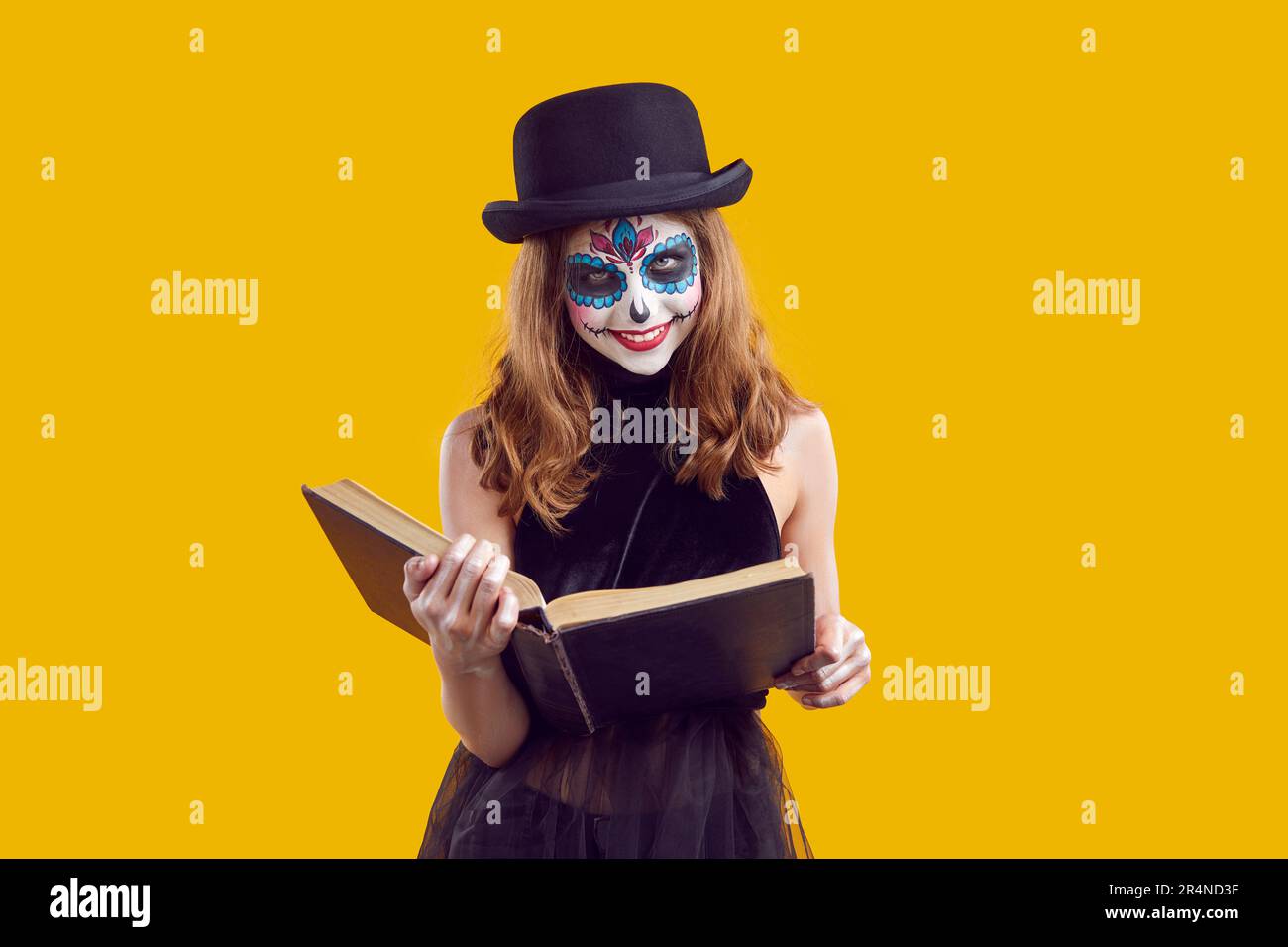 Happy, smiling, tricky girl in black suit and witch hat with skull ...