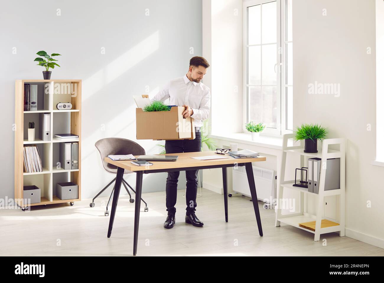 Fired male office worker standing by his desk and packing his stuff in ...