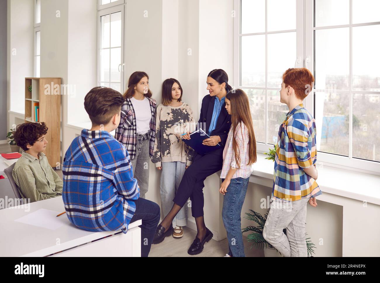 Junior school students talking to friendly female teacher during break ...