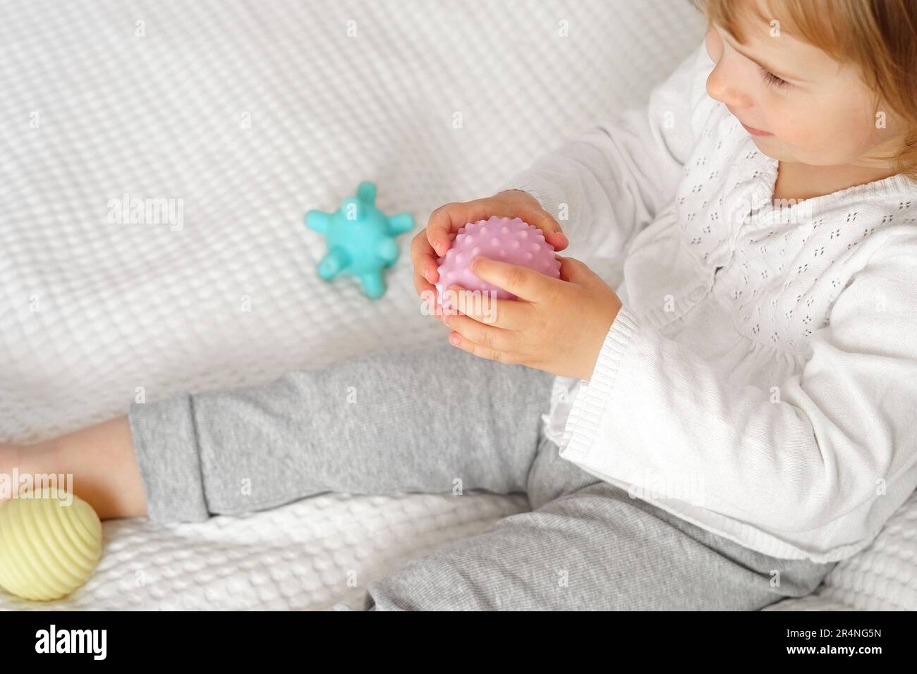 Cute baby girl playing tactile knobby balls. Young child hand plays ...