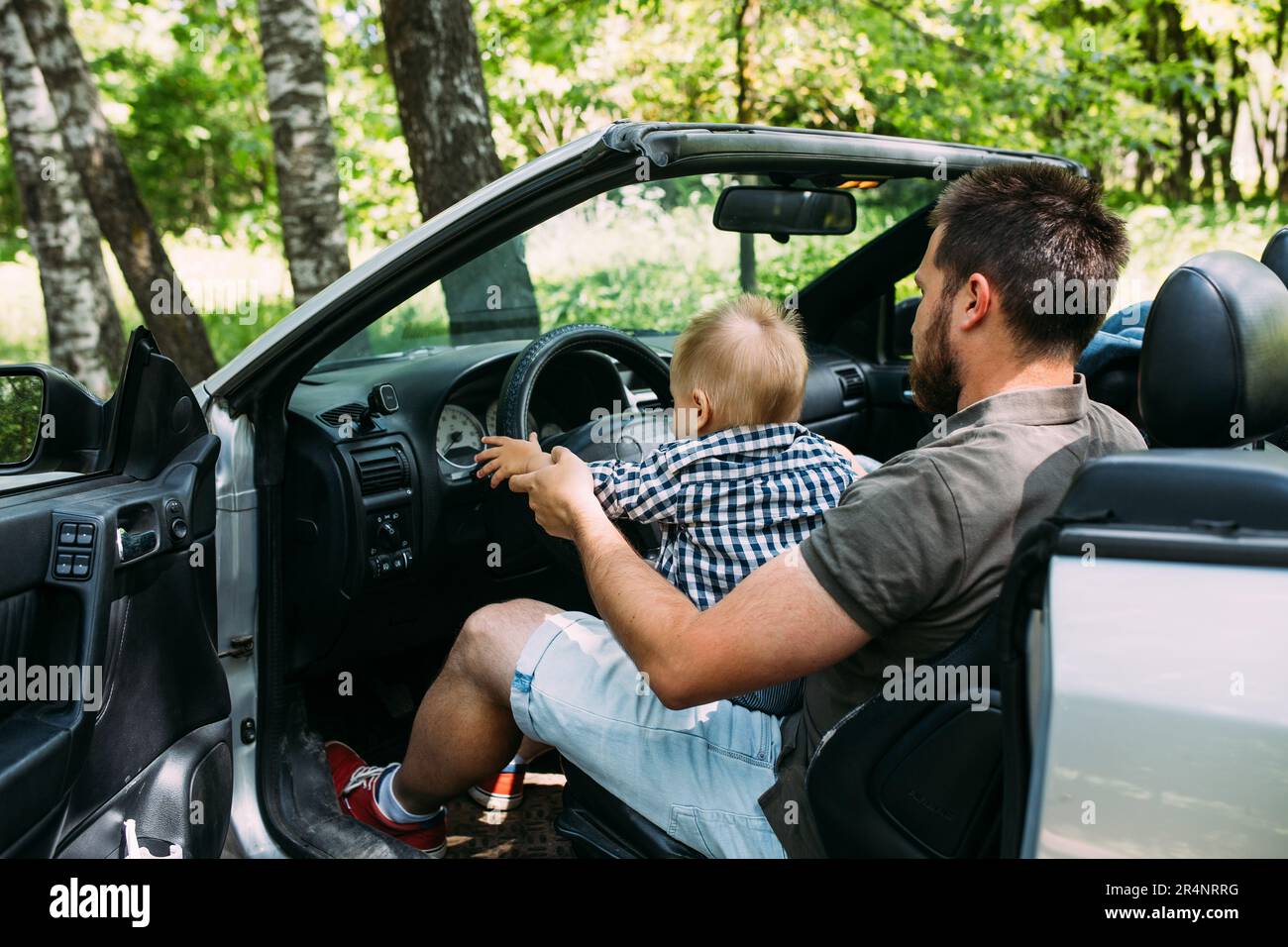 Dad shows his little son how to drive car while sitting behind wheel ...