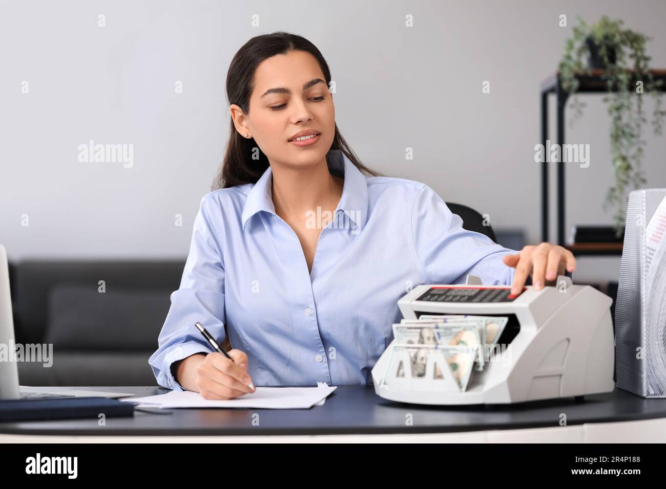 Female bank manager using cash counting machine in office Stock Photo ...