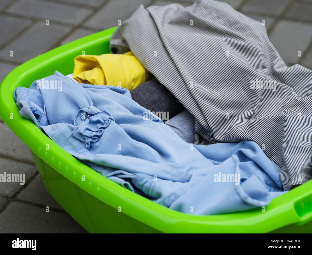 Clean dried clothes laying in a green laundry basket outdoors. Close-up ...