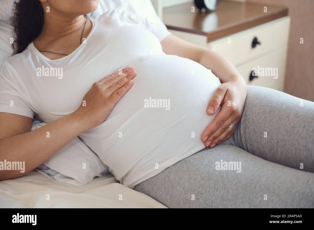 Pregnant expectant woman gently caressing her belly lying on the bed ...
