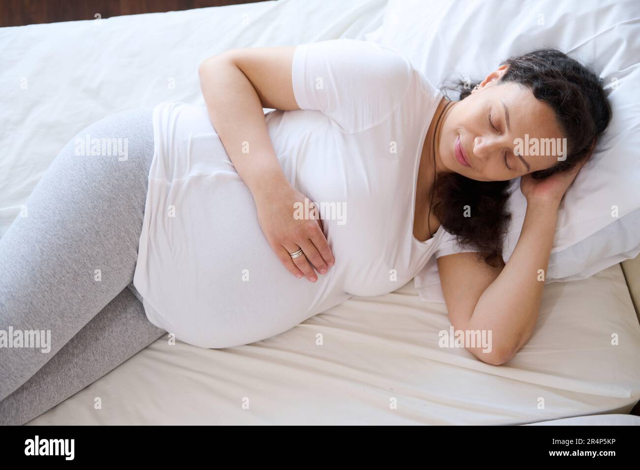Close-up top view of pregnant woman sleeping, relaxing on the bed ...