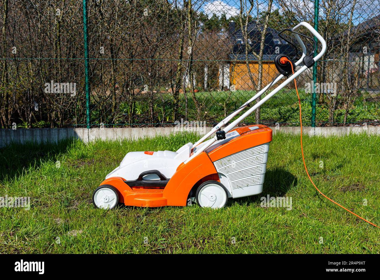 A small motorized electric mower standing on the lawn, it is orange in ...