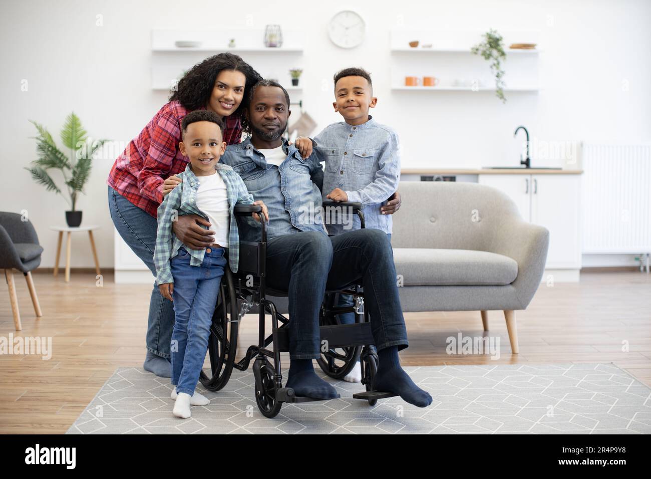 Full length portrait of happy multicultural family of four hugging each other while posing in ...