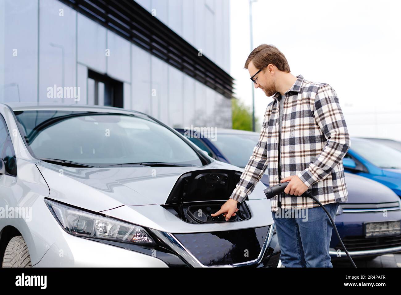 Young man plugging charging cable into the car socket. Electric car ...