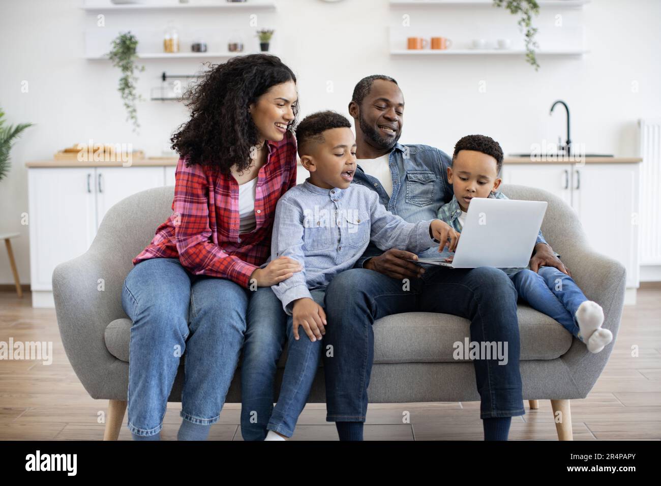 Affectionate african american mom tickling one of cute sons while happy father showing video to ...