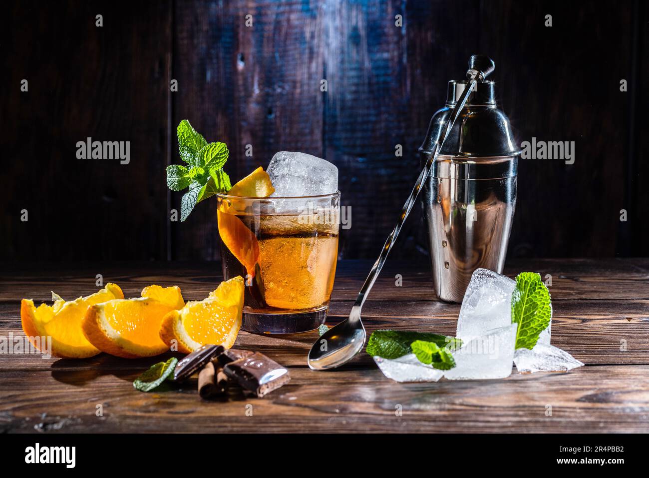 A glass of whiskey and a large ice cube. Steel shaker and bartender's ...