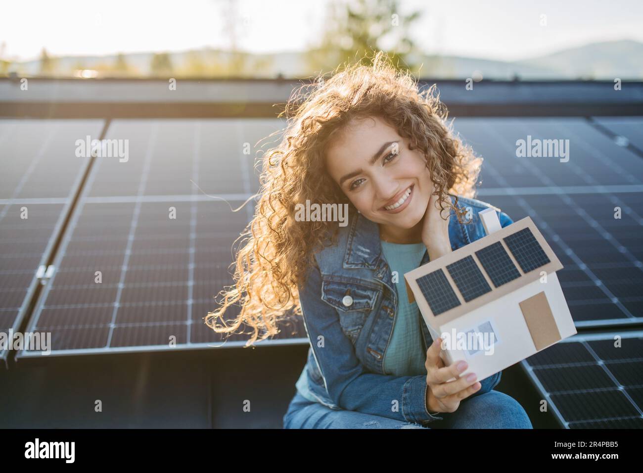 Portrait of young woman on roof with solar panels, holding model of ...