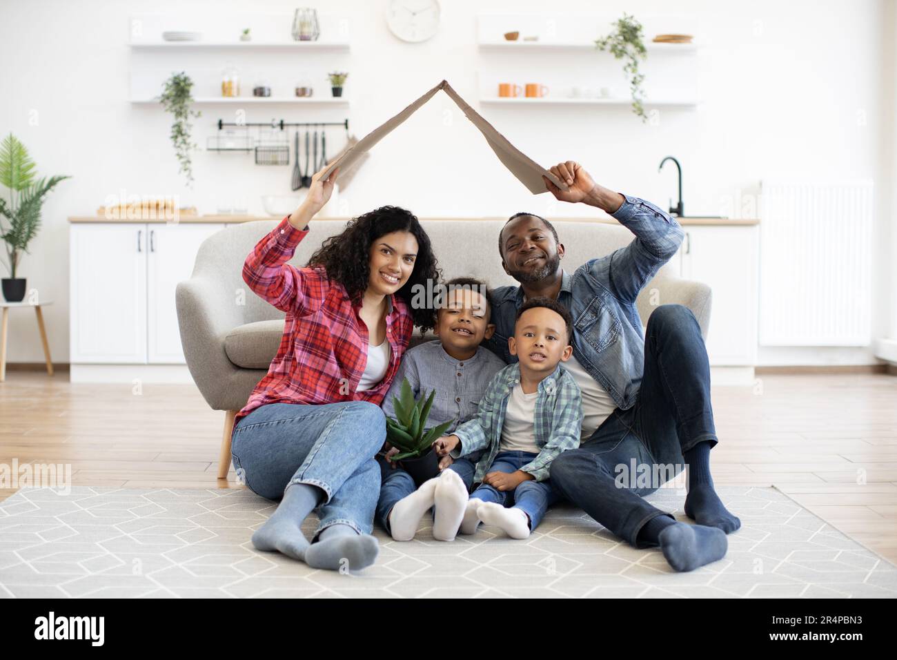 Multicultural family holding cardboard box above heads in form of house ...