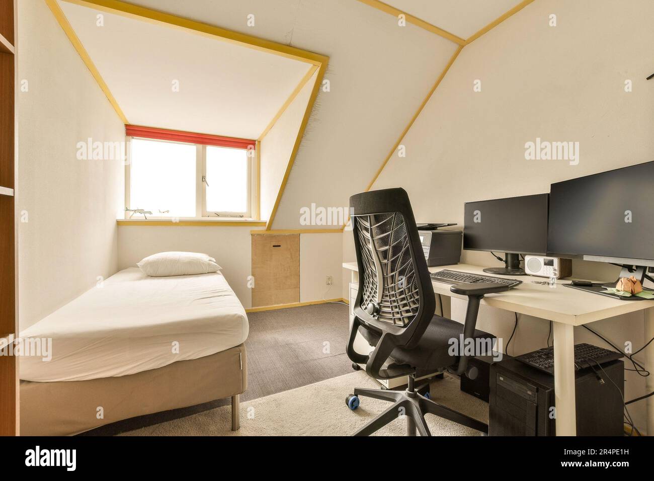 a room with a bed, desk and two computer monitors on the wall next to ...