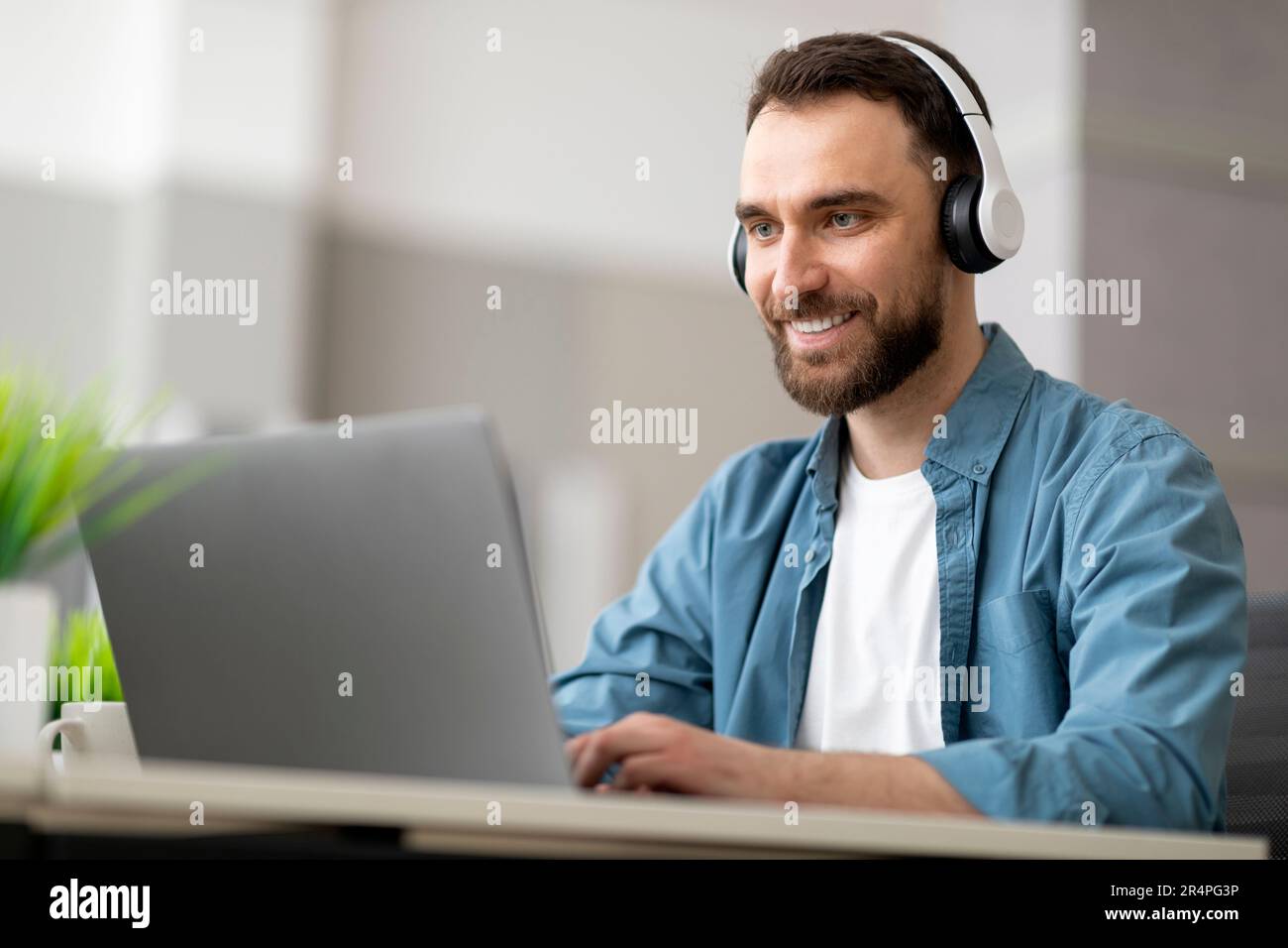 Smiling male employee wearing wireless headphones working on computer ...