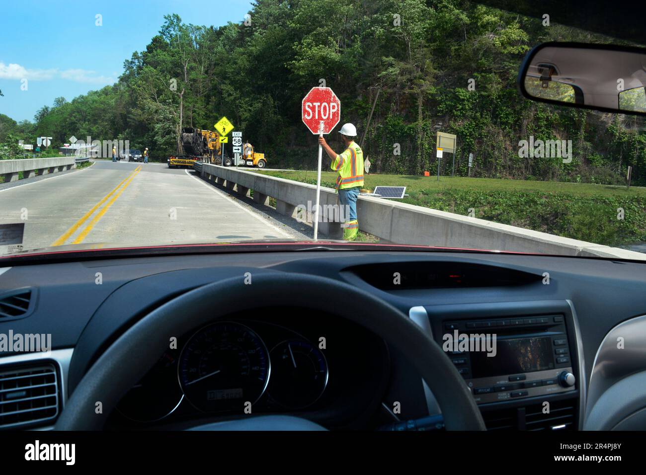 A flagman stops traffic on a highway to allow a truck hauling a wide ...