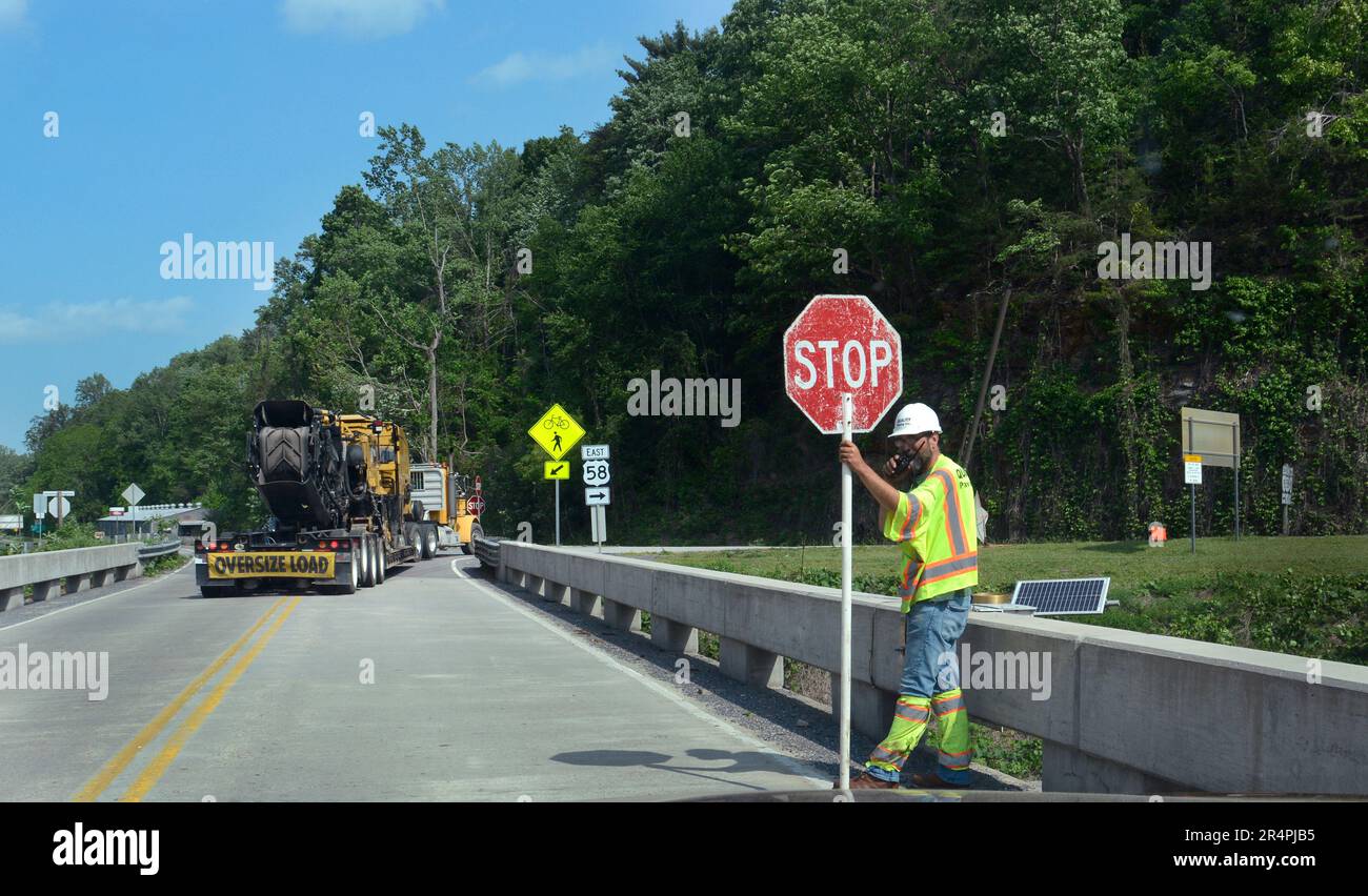 A flagman stops traffic on a highway to allow a truck hauling a wide ...