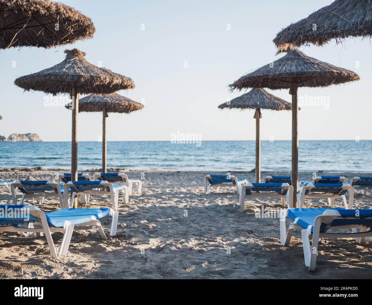 Sandy beach with blue sunbeds and straw umbrellas and the sea at the ...