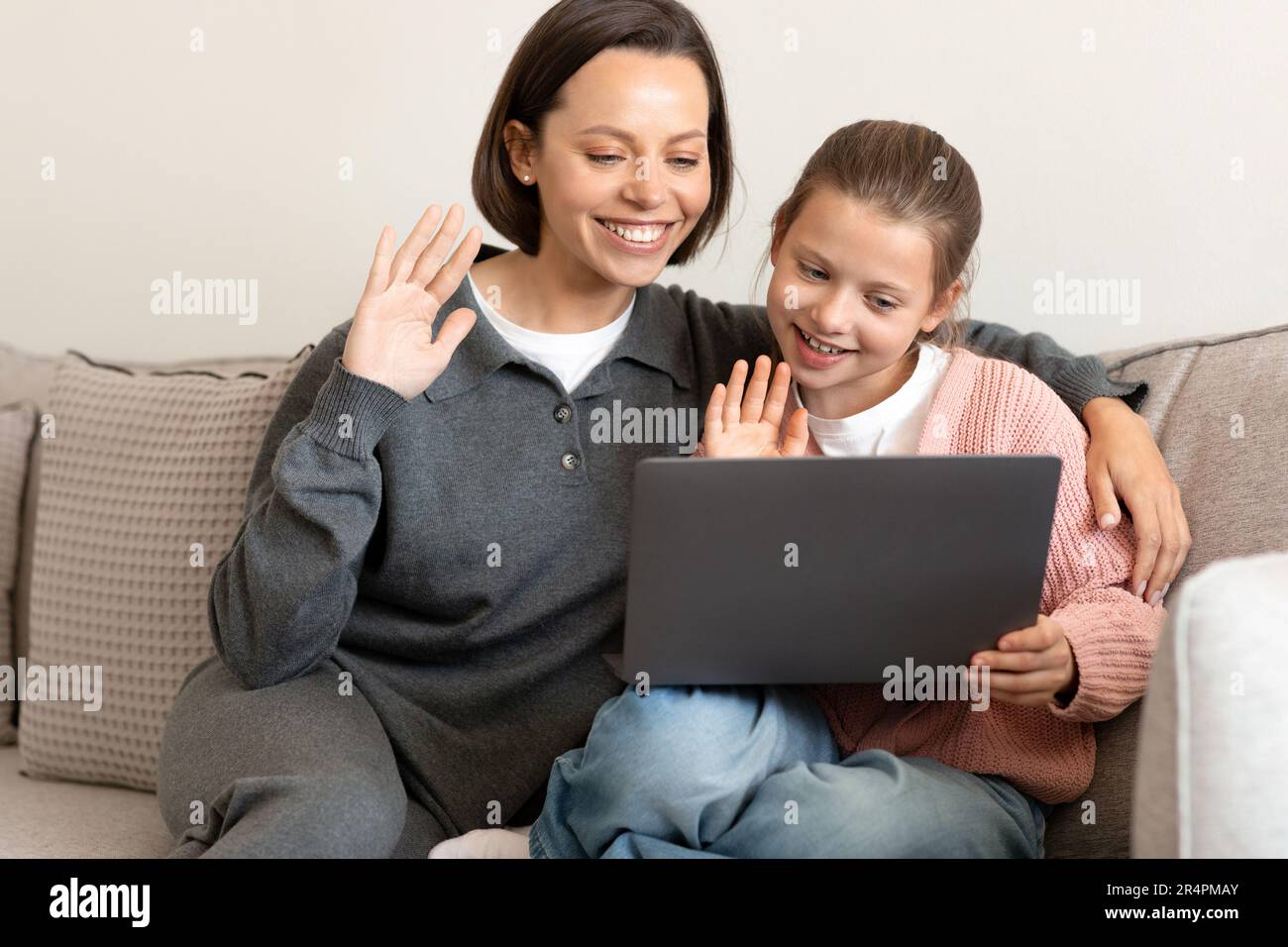 Cheerful caucasian middle aged mom and little daughter wave hands, look at computer, greeting ...